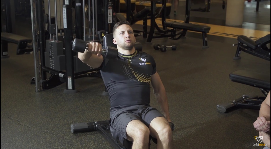 Unoszenie ramion z hantlami w przód siedząc (naprzemienne) - BudujMase.pl