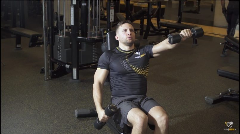 Unoszenie ramion z hantlami w przód siedząc (naprzemienne) - BudujMase.pl